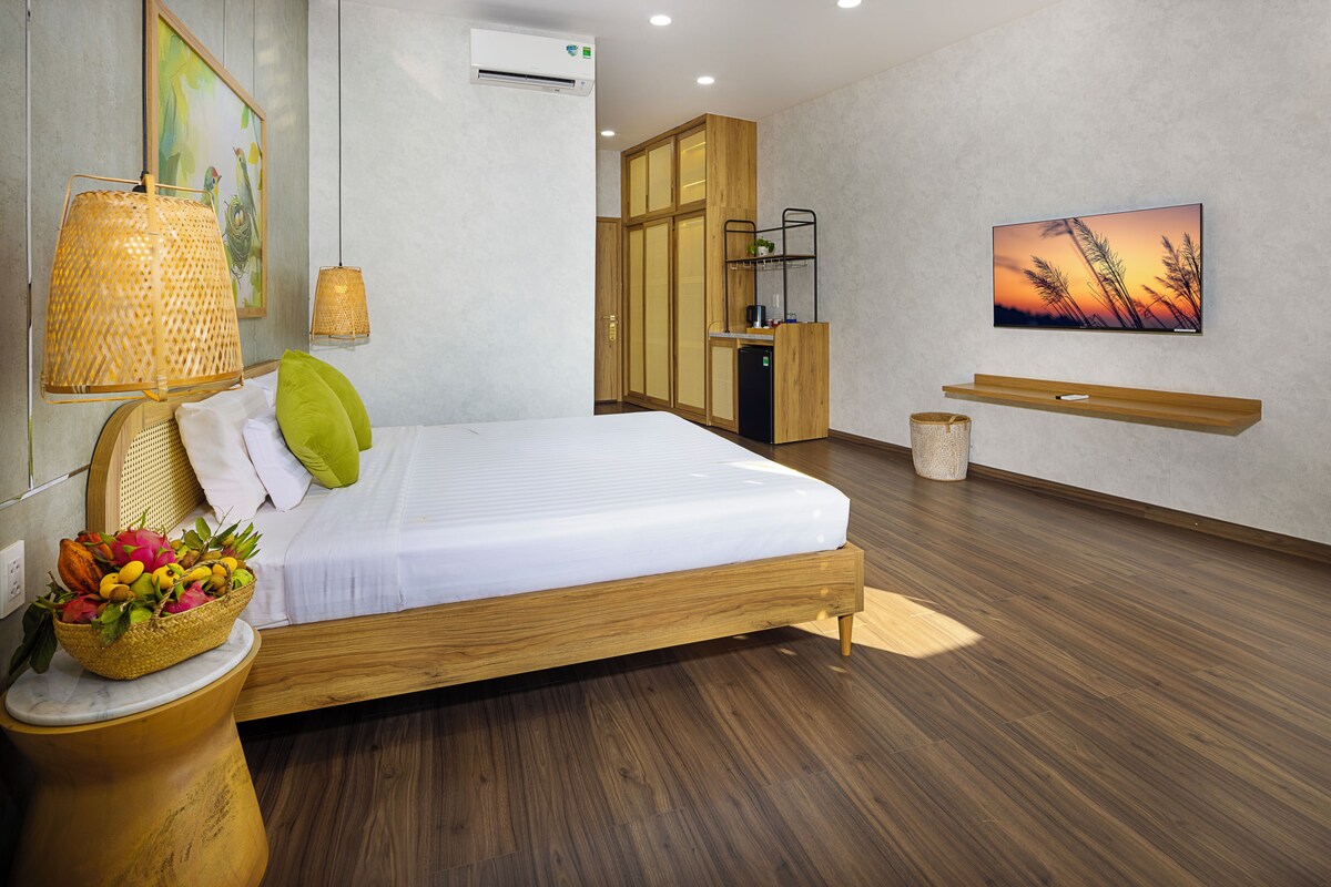 Quarto de hotel moderno com cama de madeira, uma pequena escrivaninha, televisão e ar condicionado fixado na parede.