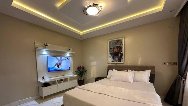 Quarto de hotel moderno com uma cama grande, televisão de tela plana, mesa de cabeceira e luminária de teto.