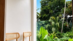 Quarto com duas cadeiras de madeira com almofadas verdes, uma pequena mesa de madeira e um candeeiro pendente.