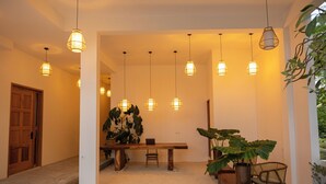Uma sala de jantar com mesa de madeira, cadeiras, luminárias pendentes e plantas em vasos.