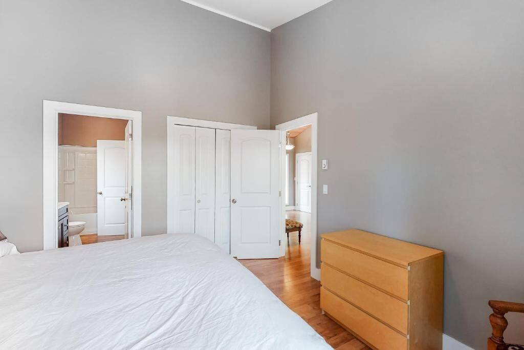 Quarto com uma cama, cômoda e duas portas que dão para outros ambientes.