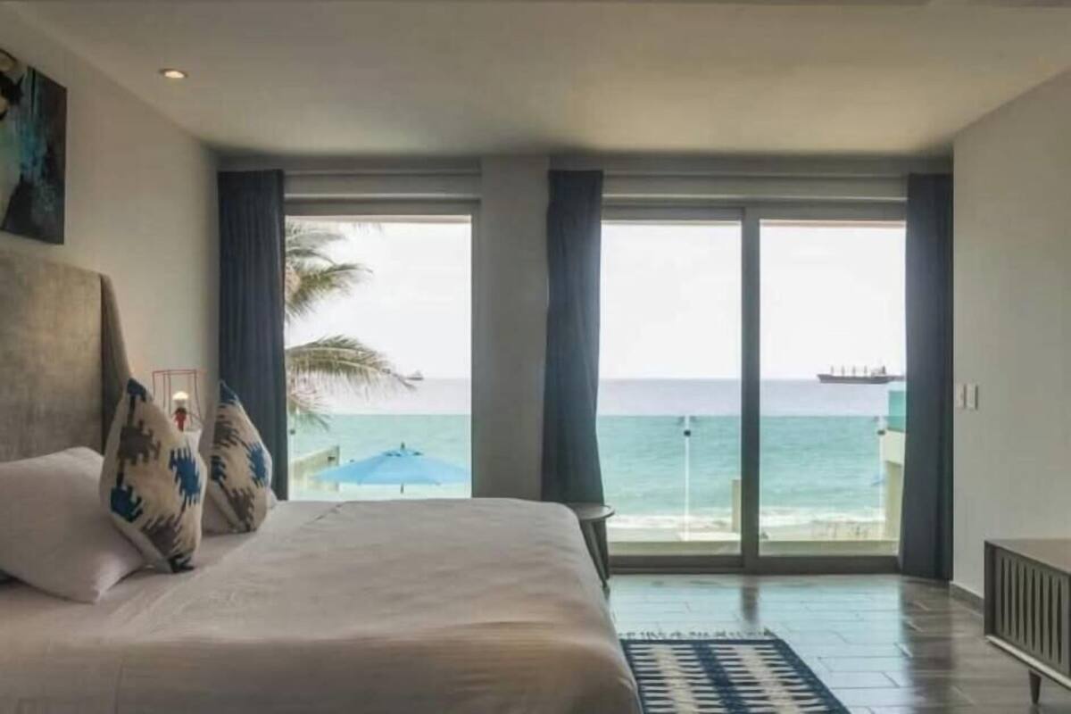 Quarto com uma cama grande, vista para o oceano e um navio ao longe.