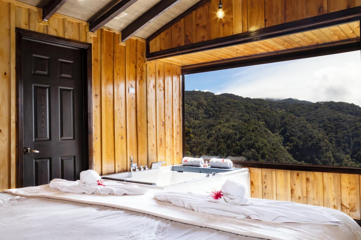 Quarto de madeira com uma janela grande, uma porta preta e uma cama com toalhas.