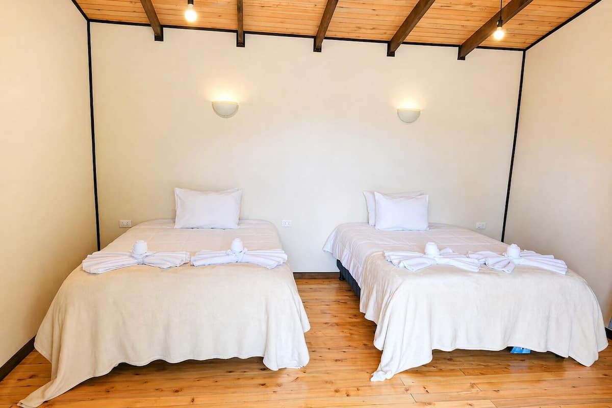 Quarto com duas camas, cada uma com roupa de cama e toalhas brancas, piso de madeira e teto de madeira com vigas aparentes.