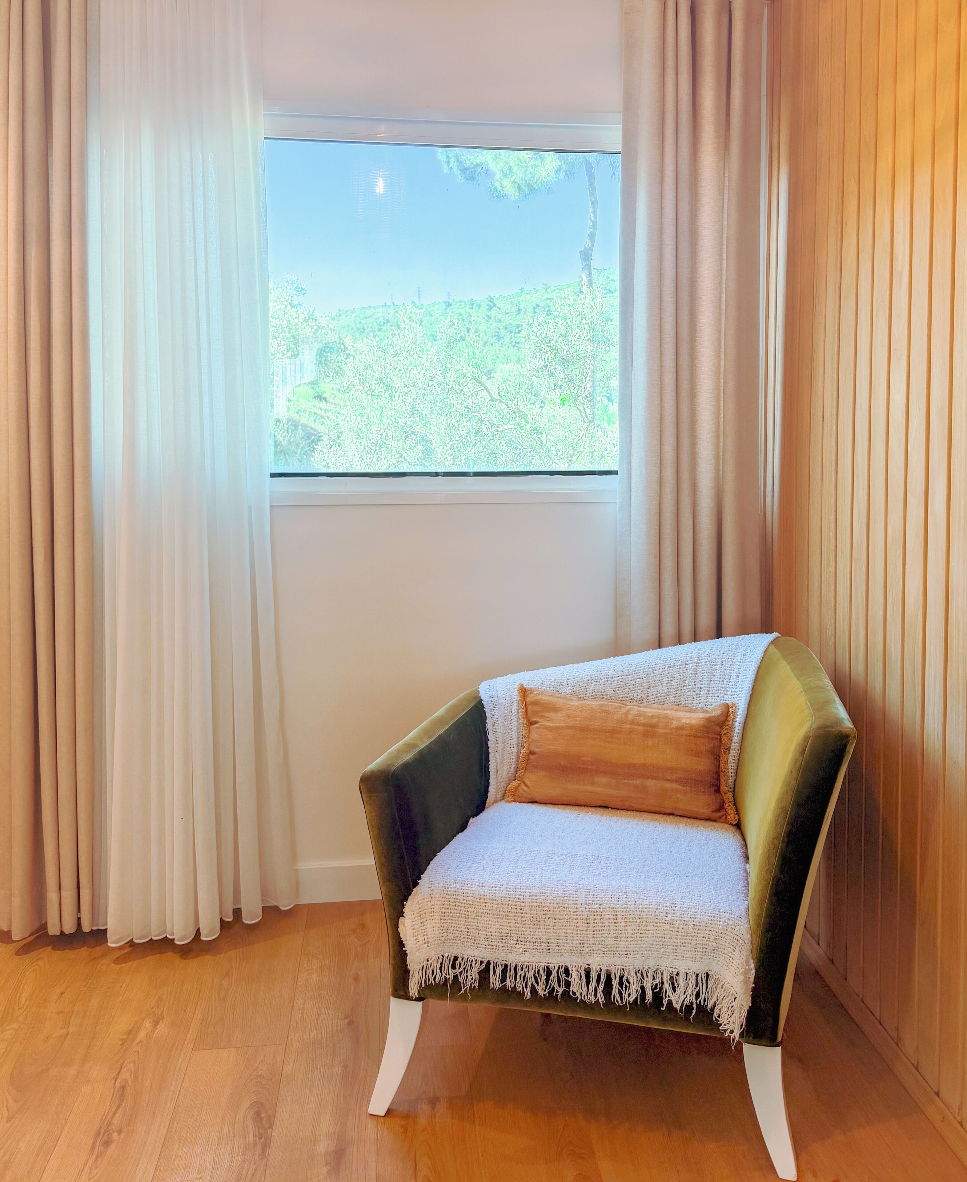 Quarto de canto com janela, uma cadeira e piso de madeira.