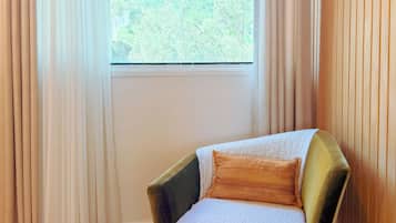 Quarto de canto com janela, uma cadeira e piso de madeira.