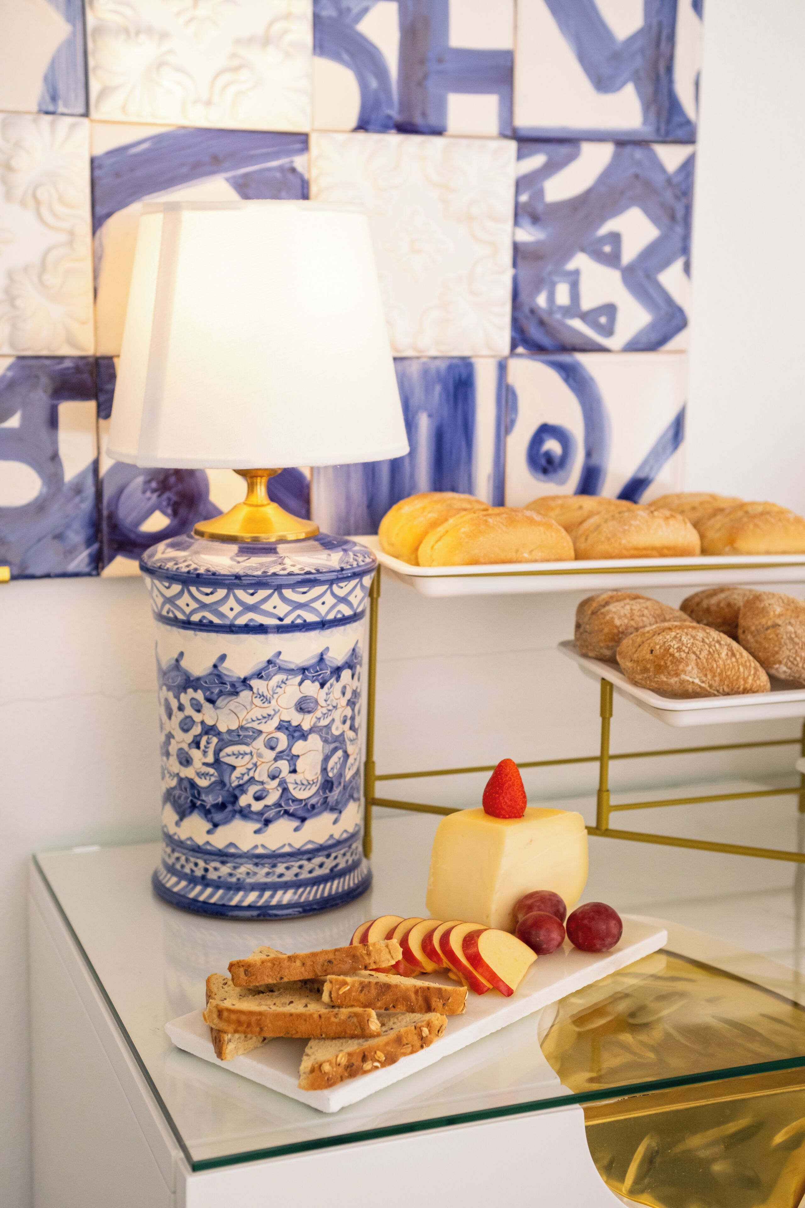Uma mesa com uma lâmpada decorativa, queijo, frutas e doces.