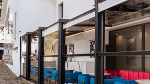 Um café com mesas ao ar livre, um caminho de pedras e um edifício branco com obras de arte na parede.