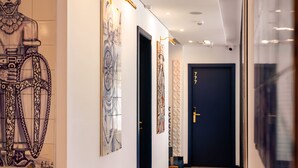 Um corredor com obras de arte nas paredes, uma porta escura com o número 777 e um lustre moderno.