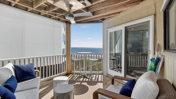 Varanda com vista para o mar, mobiliário de exterior branco e porta de vidro que dá para uma área interior.