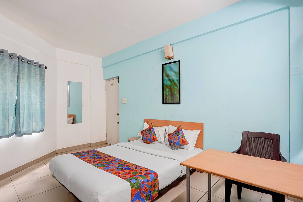 Quarto de hotel com cama, escrivaninha, cadeira, espelho e porta.