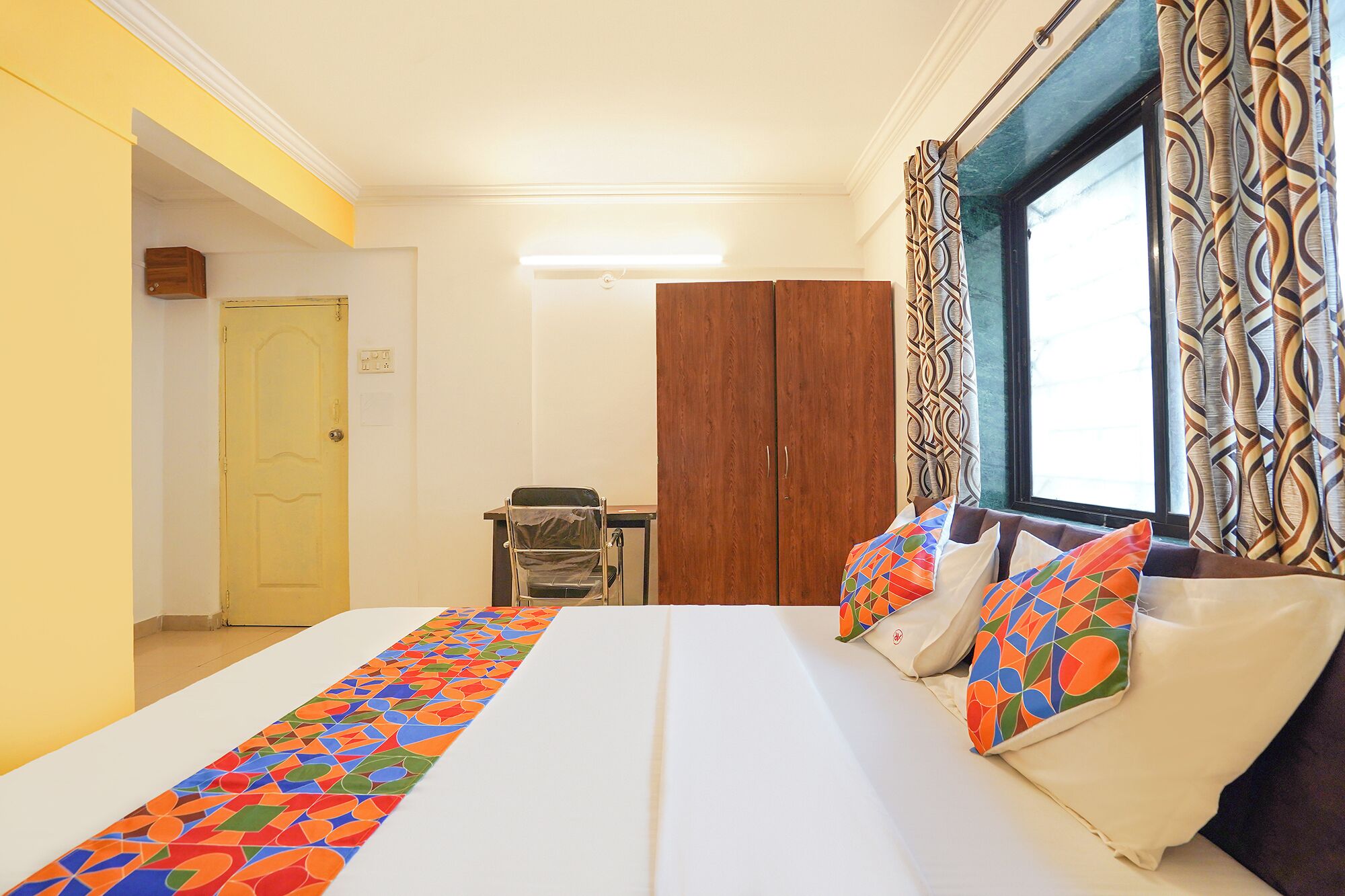 Quarto de hotel com cama, escrivaninha e guarda-roupa.