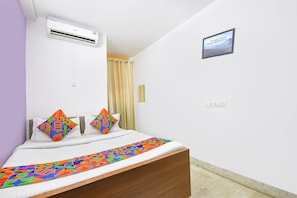 Quarto com cama, almofadas coloridas, aparelho de ar condicionado, tomada e uma frase motivacional na parede.