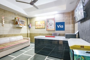 Quarto de hotel com sofá, balcão de recepção, ventoinha no teto e decorações fixadas na parede.