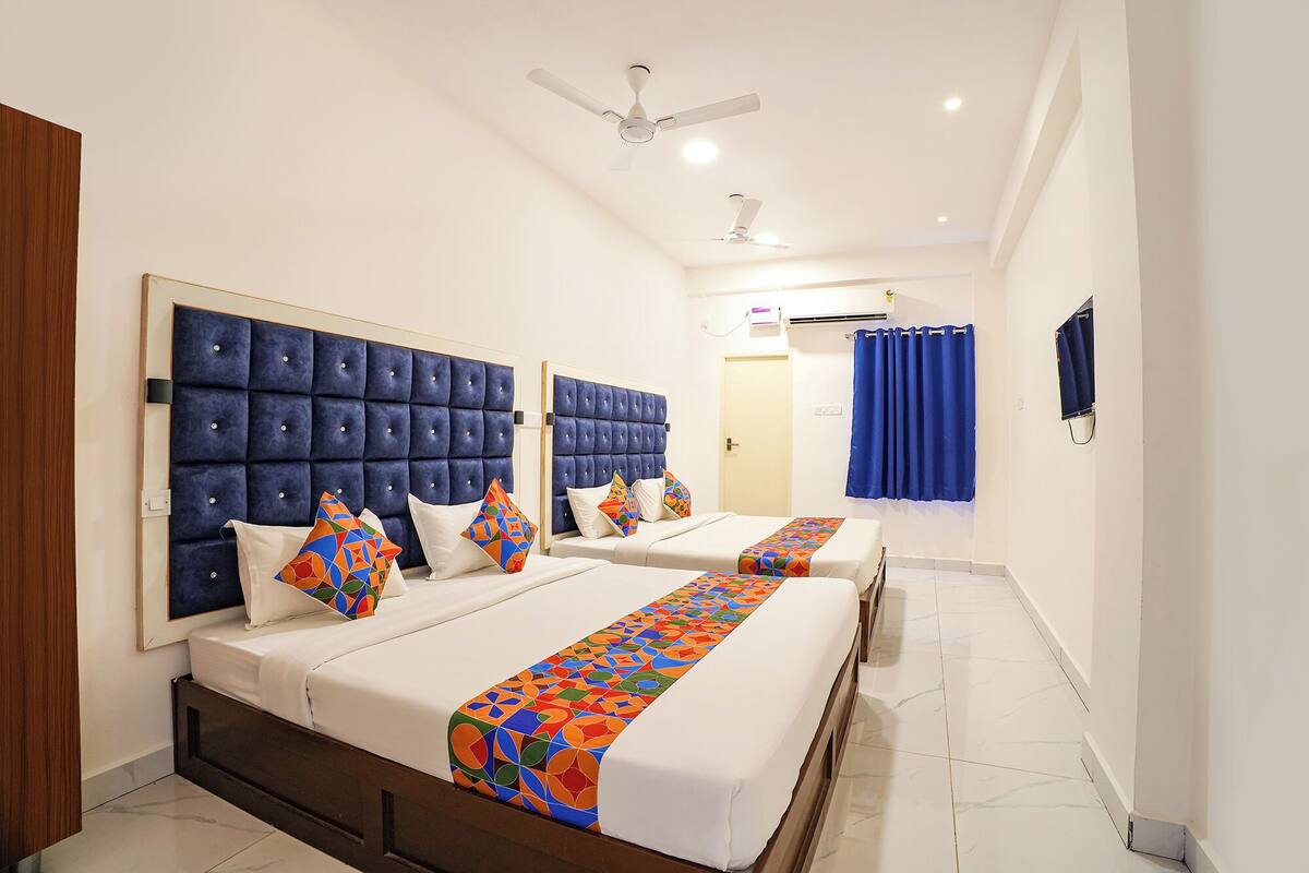 Quarto de hotel com duas camas, um ventilador de teto, banheiro com cortina de chuveiro e piso em azulejos.