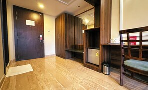Quarto de hotel com armário de madeira, mini-geladeira, lixeira e uma cadeira.