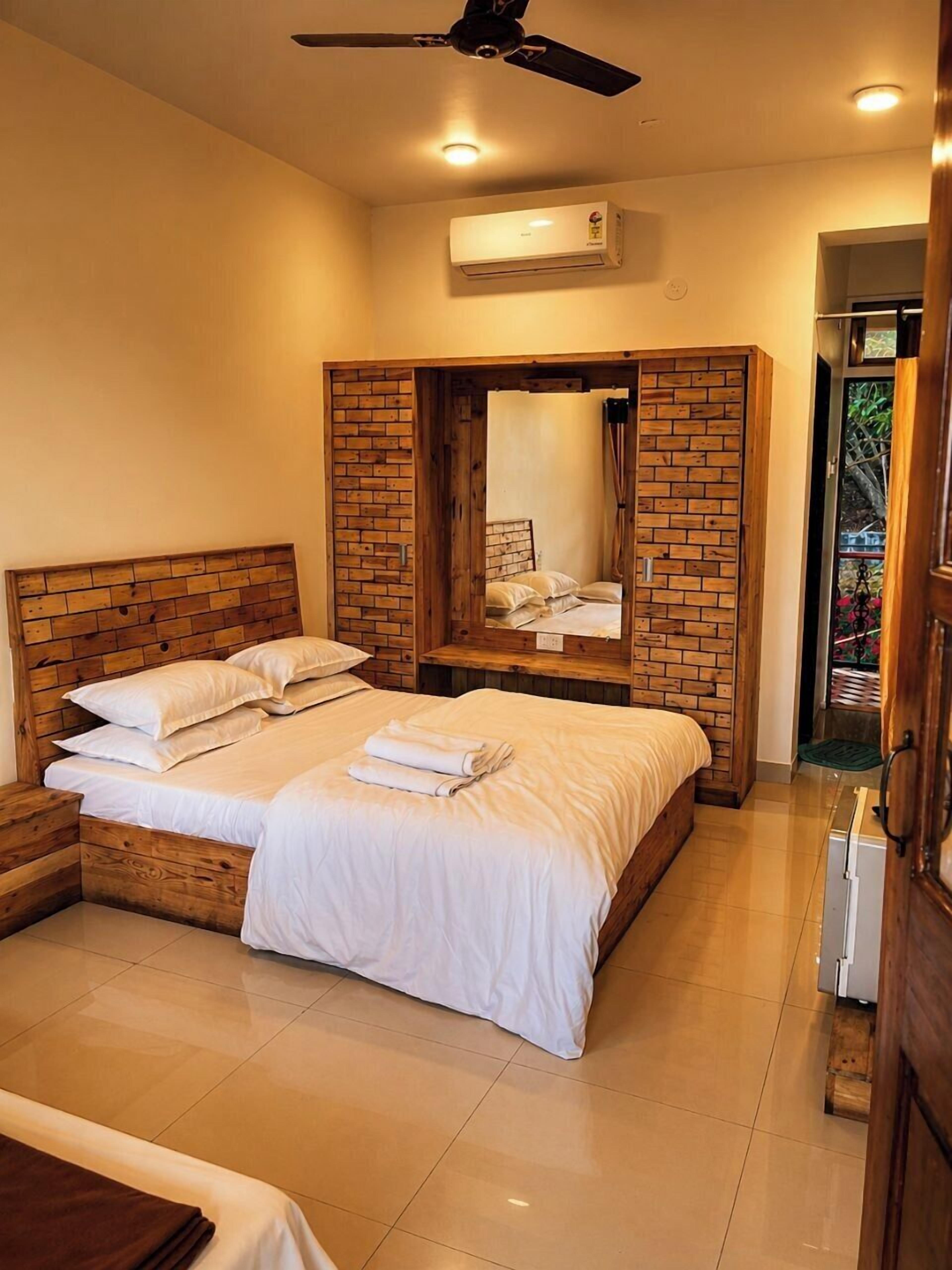Quarto com duas camas, ventilador de teto, ar condicionado e armário de madeira.