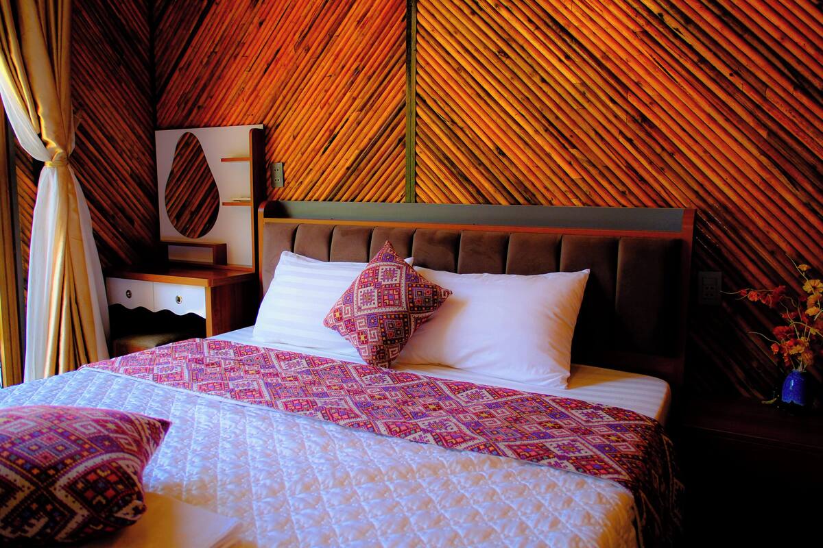 Uma cama com roupa de cama estampada, cabeceira de madeira e mesa de cabeceira com um vaso de flores.