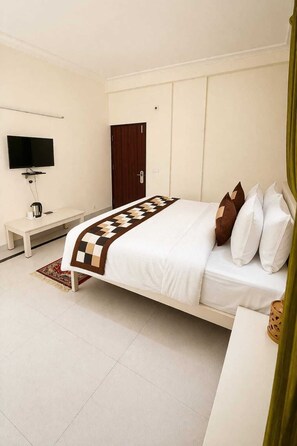 Quarto de hotel com cama, televisão, escrivaninha e guarda-roupa.