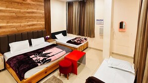 Quarto de hotel com uma cama grande, uma cama menor, uma escrivaninha e um ventilador de teto.