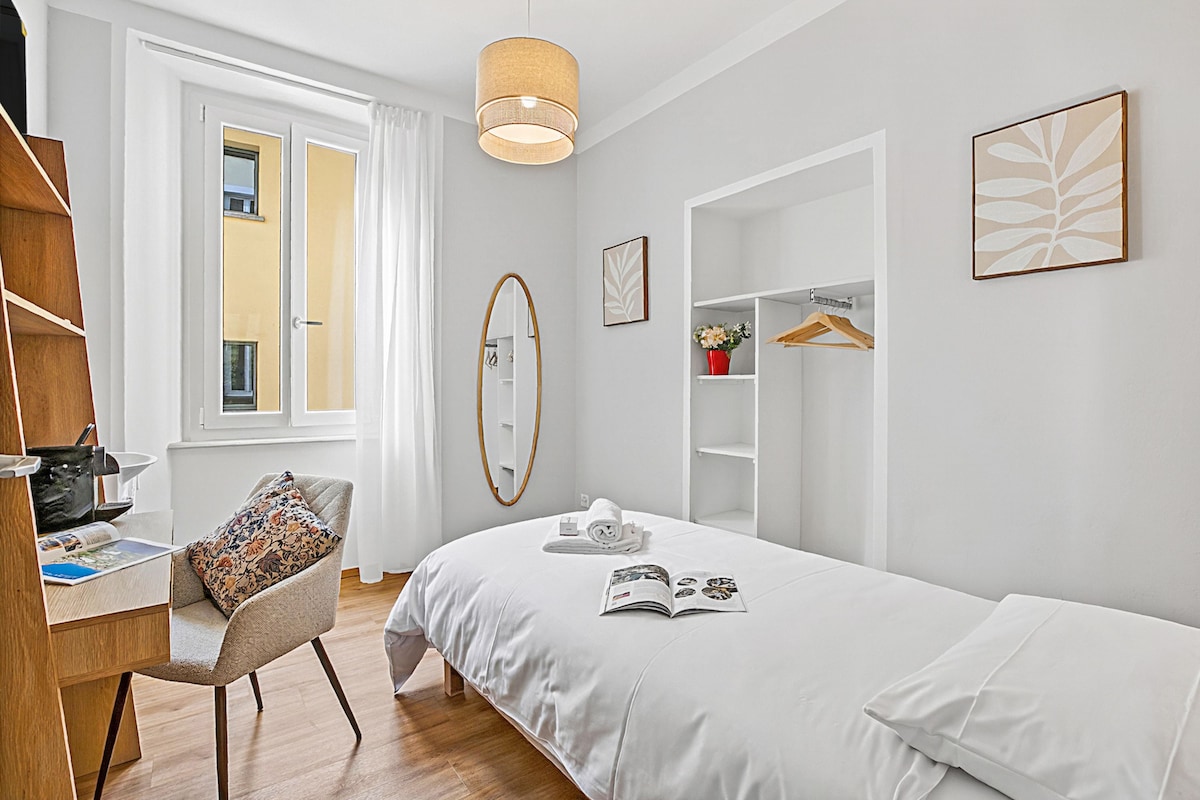 Quarto com cama, cadeira, escrivaninha, guarda-roupa e luminária suspensa.