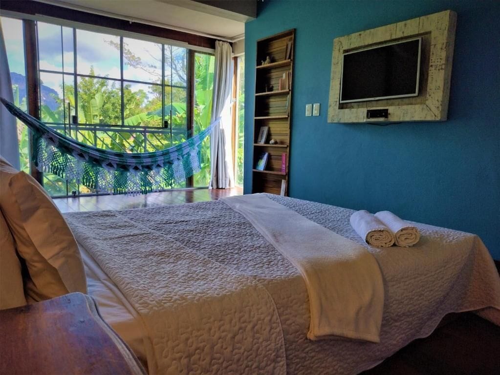 Quarto com uma cama grande, uma rede, uma televisão e uma estante de livros.