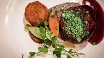 Prato com carne como peça central, um item frito e guarnição de folhas verdes.