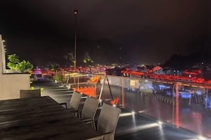 Terraço com mesa e cadeiras, de frente para um corpo d'água com barcos iluminados.