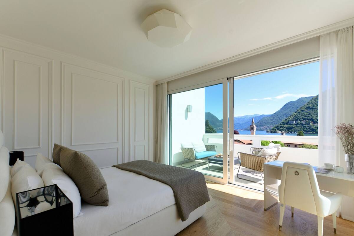 Quarto com cama, escrivaninha e vista para o exterior.