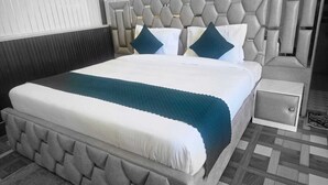 Quarto de hotel com uma cama grande, cabeceira com padrão geométrico, mesa de cabeceira e piso estampado.