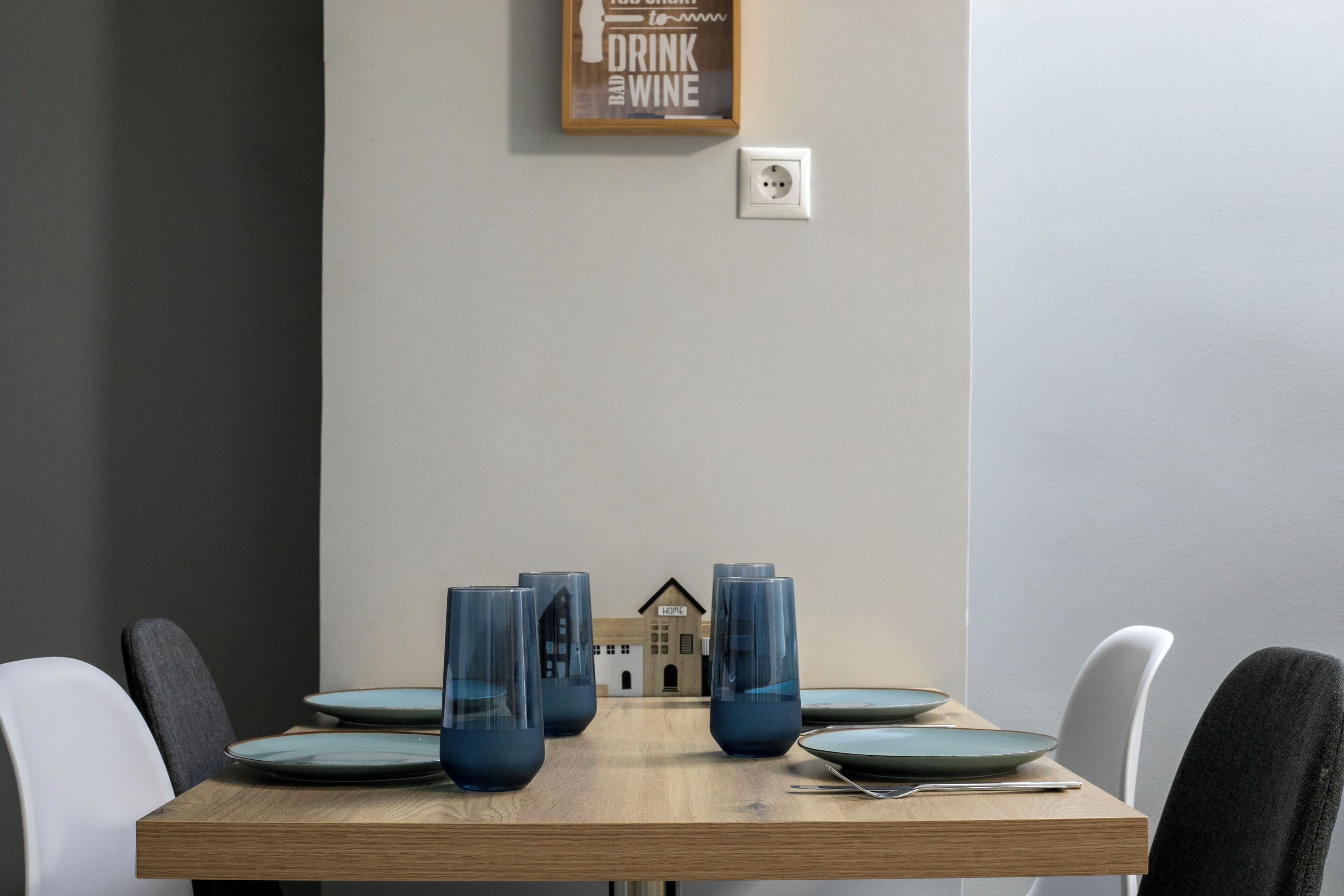 Uma mesa de jantar com quatro copos e pratos azuis, um modelo de casa na parede e uma tomada.