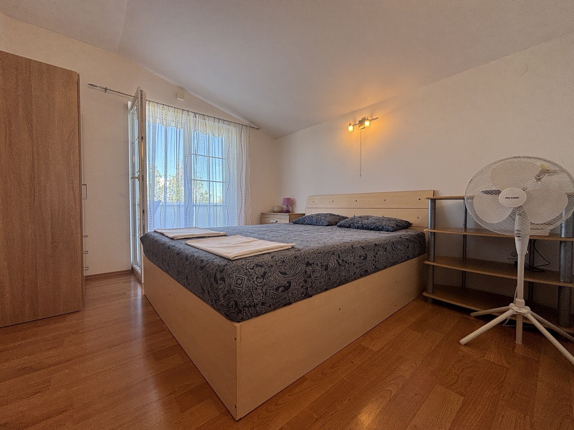 Quarto com cama, ventilador, janela com cortinas e porta.