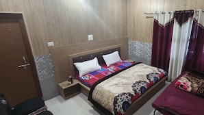 Quarto com cabeceira de madeira, cama com roupa de cama estampada, mesa de cabeceira e uma cadeira.