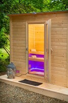Estrutura de sauna de madeira com a porta aberta, mostrando um banco e um suporte para toalhas no interior.