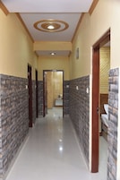 Um corredor com piso de azulejos, uma porta de madeira à direita e um banheiro visível por uma porta aberta ao fundo.