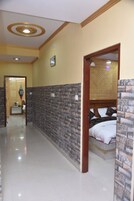 Corredor de hotel com parede em padrão de tijolos, moldura de porta de madeira e cama com cabeceira estampada.