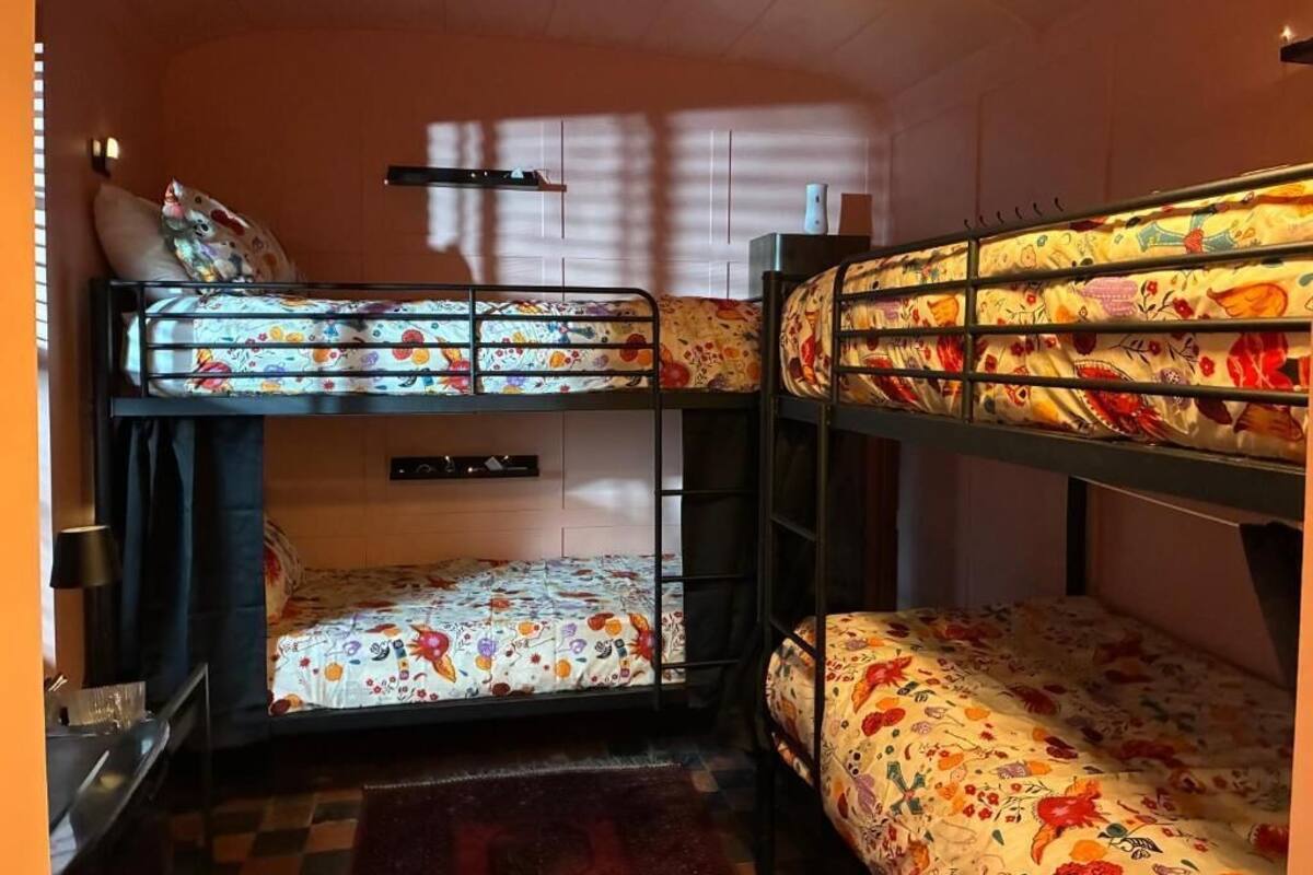 Quarto com beliche, piso xadrez, uma mesinha com abajur e uma janela com persianas.