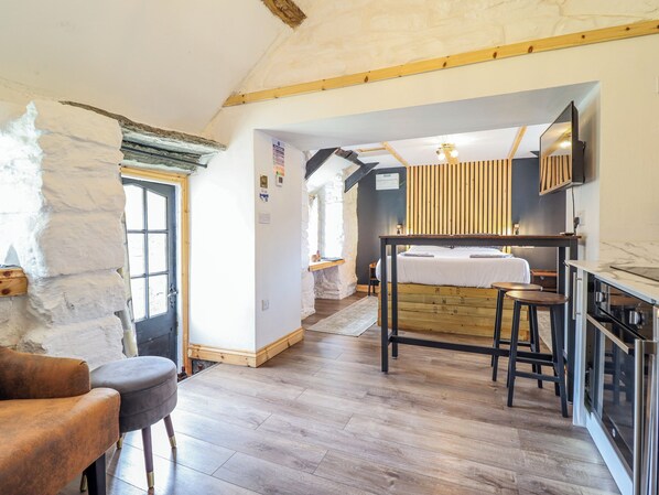 Quarto com cama, mesa de madeira, espaço de cozinha e parede de pedra.