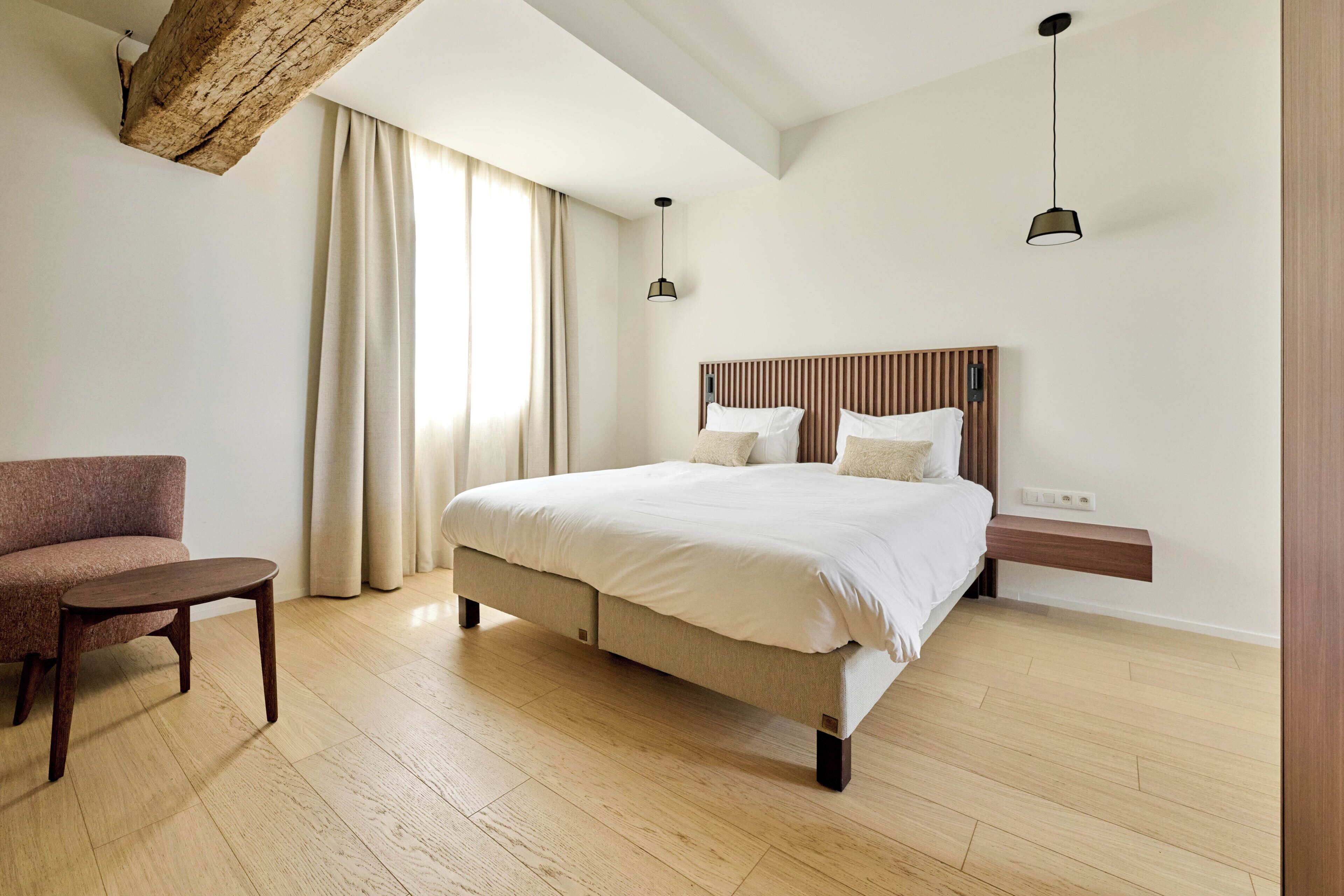Quarto com cama, uma cadeira, luminária pendente e janela com cortinas.