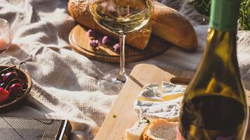 Disposição para piquenique com um copo de vinho branco, queijo, pão e um livro sobre uma manta.