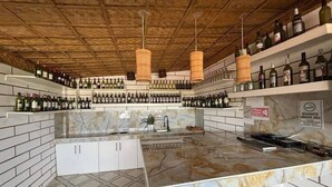 Uma área de bar com bancada de mármore, luminárias de vime suspensas e prateleiras cheias de garrafas de vinho.