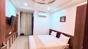 Quarto de hotel com cama, ventilador de teto, ar condicionado, televisão e porta.