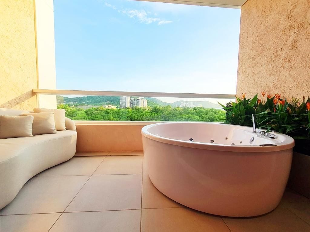 Um banheiro moderno com uma banheira grande, um sofá e vista para áreas verdes e edifícios.