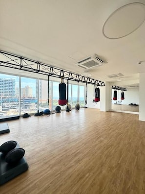 Uma academia ampla com grandes janelas, ventiladores de teto e diversos equipamentos de exercício.