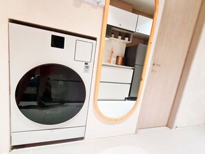 Quarto compacto com máquina de lavar, pequena cozinha e espelho.