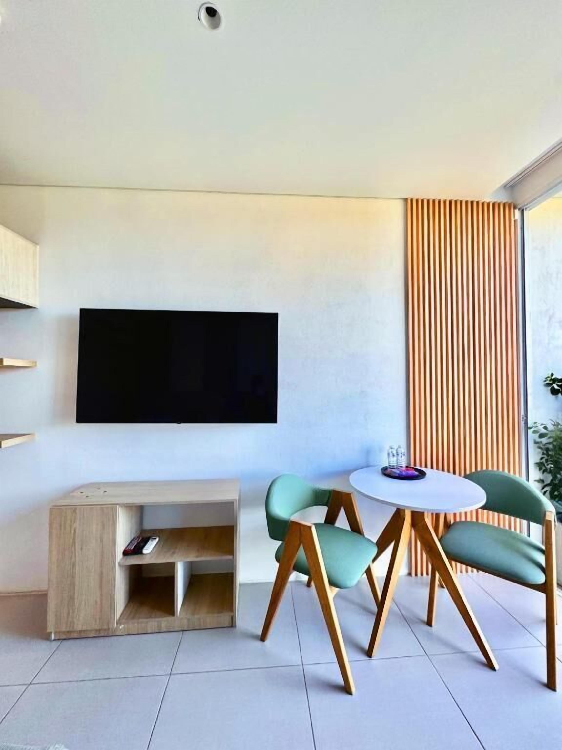 Uma sala de estar moderna com uma televisão de tela plana, um armário de madeira, duas poltronas verdes e uma pequena mesa com uma bandeja.