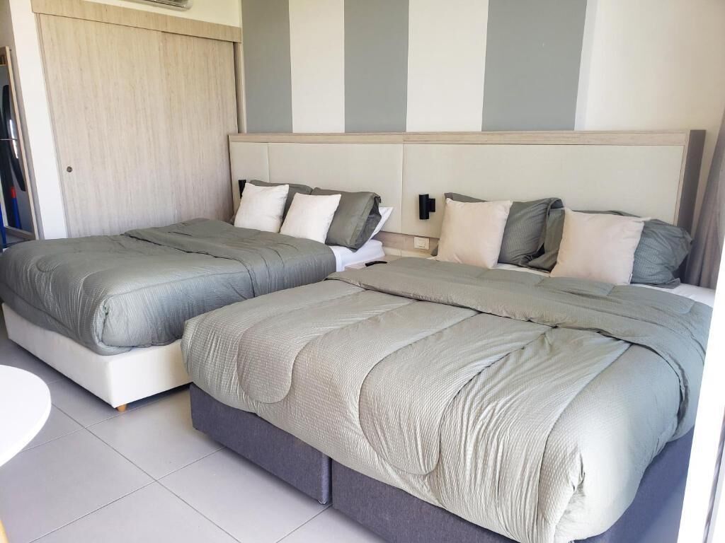 Quarto de hotel com duas camas, um guarda-roupa e uma mesinha de cabeceira.