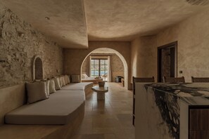 Um quarto espaçoso com um sofá grande, uma mesa de jantar e vista através de uma janela em arco.