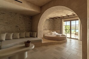 Um quarto de spa com parede de pedra, uma cama redonda, um sofá e uma janela com vista.