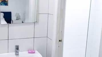 Casa de banho com lavatório branco, espelho e cabine de duche em vidro.